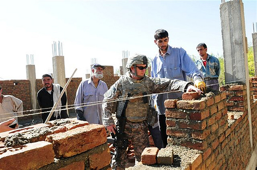Two White Men with Burdens: Laying bricks with guns